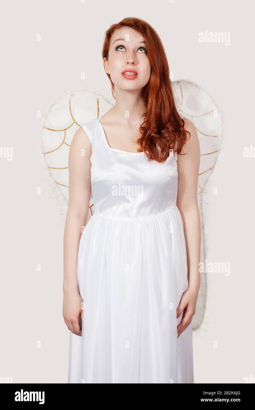Young woman dressed as an angel looking up against gray background ...