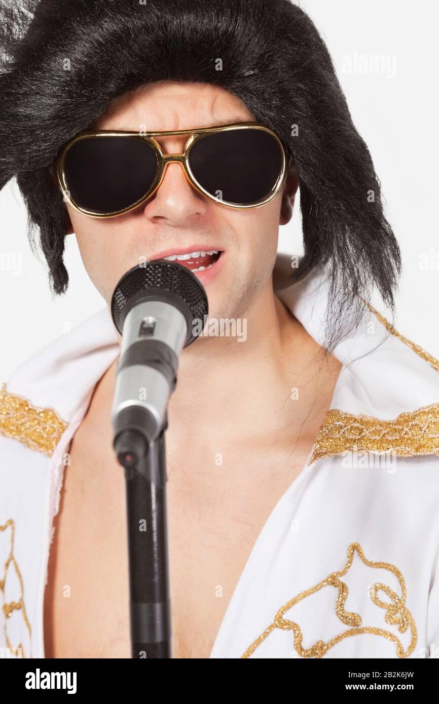 Elvis impersonator singing into a microphone against gray background ...