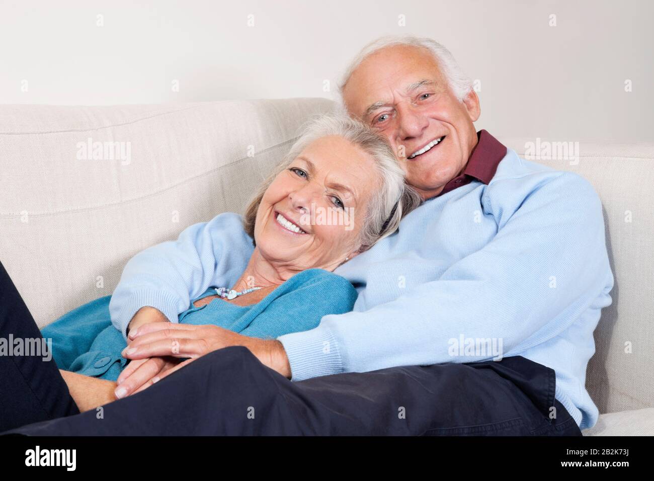 Portrait of happy elderly man with arm around spouse lying on sofa at ...