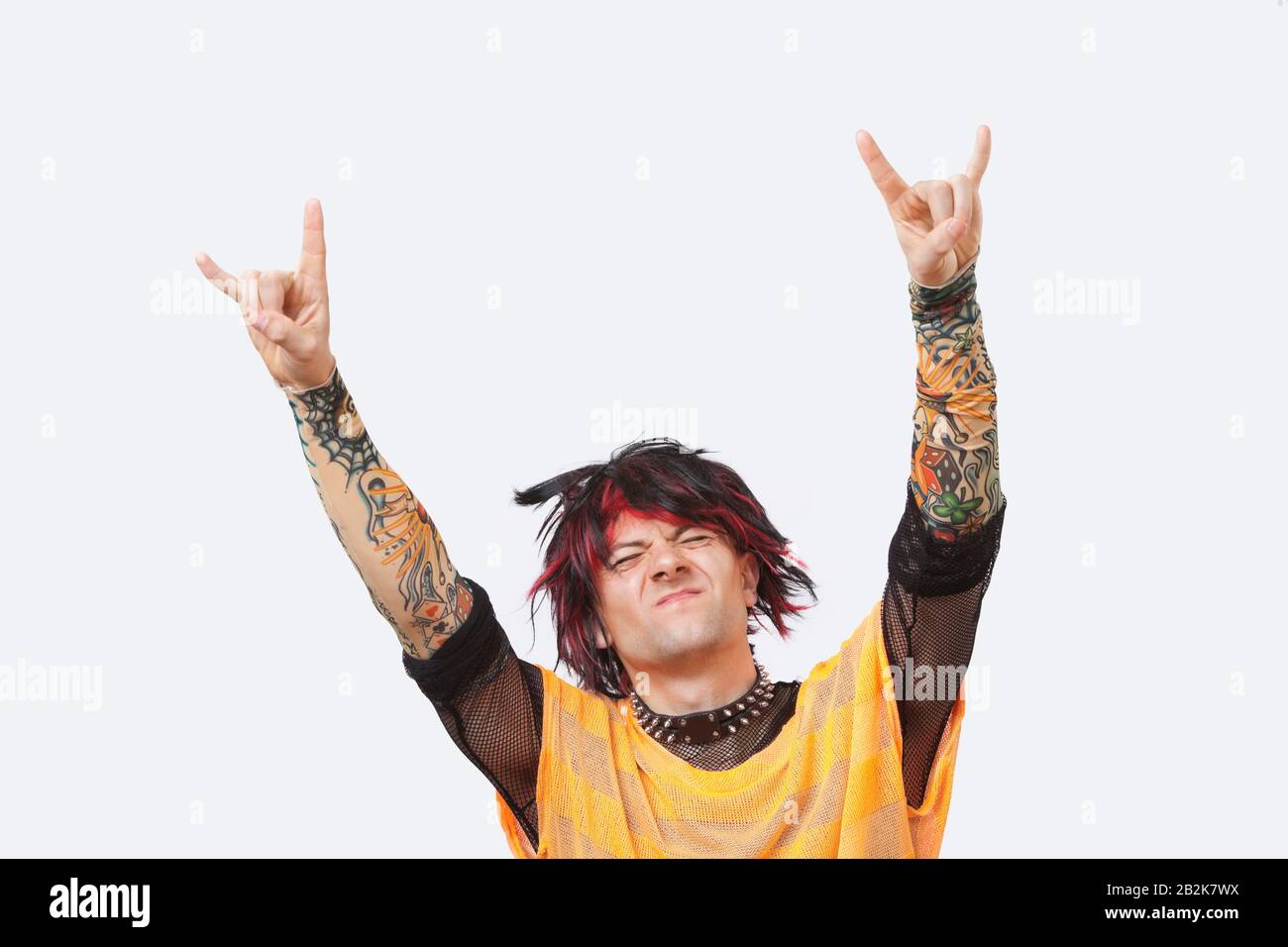 Portrait of young punk man gesturing rock & roll hand sign over white ...