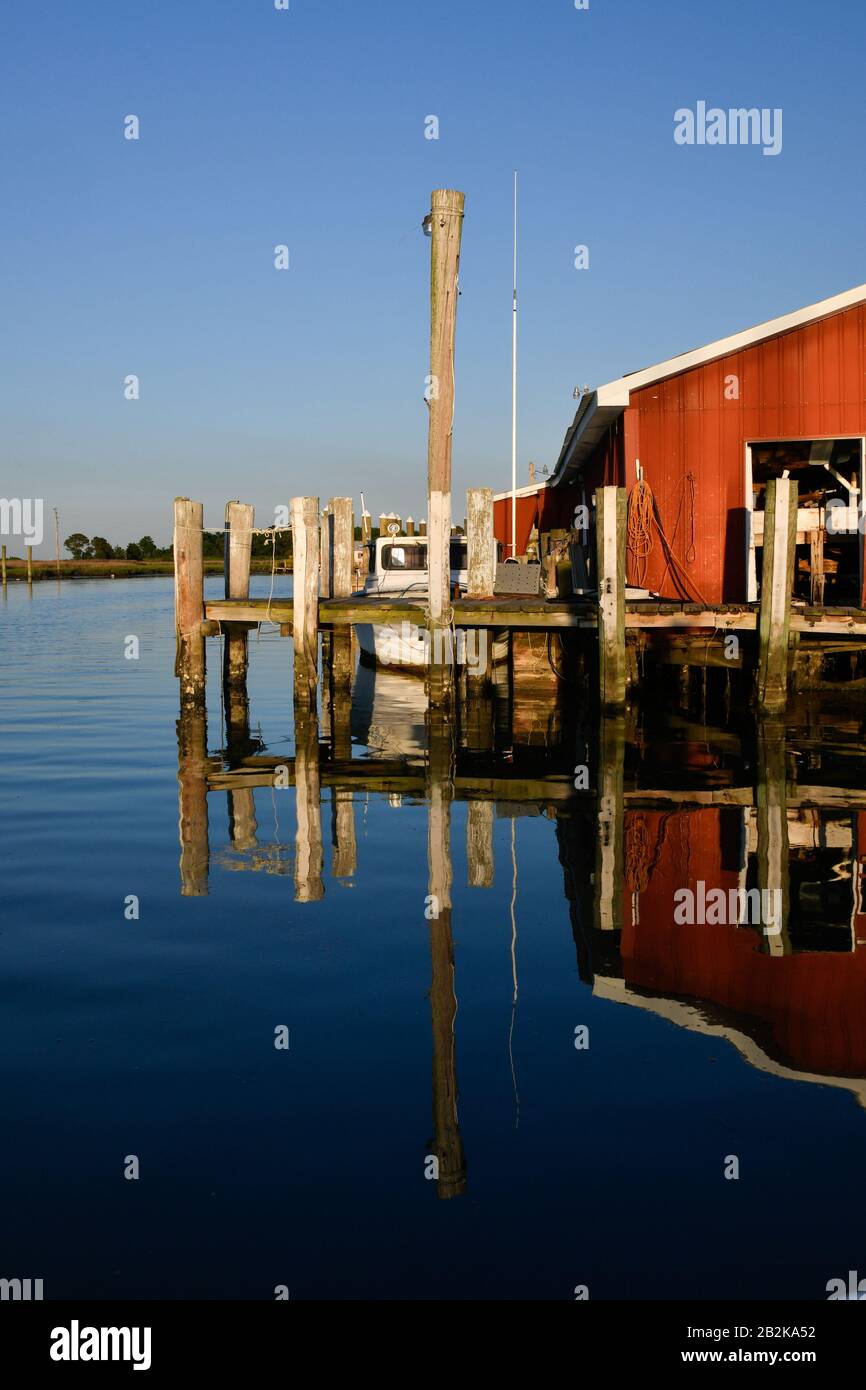 Red wooden boathouse with mirrored reflection on calm deep blue water ...