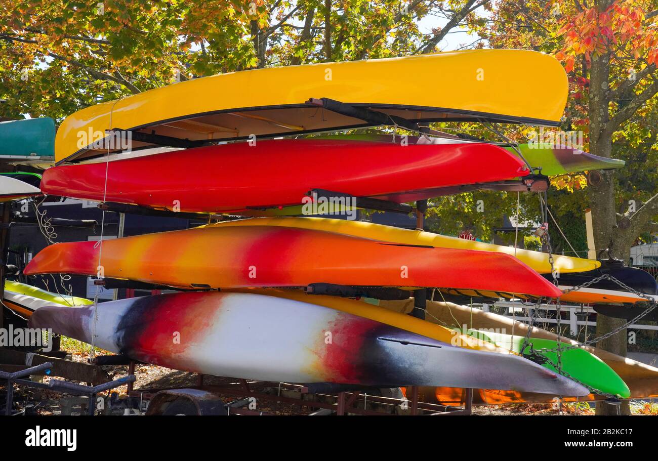 Red, yellow, green and orange kayaks stacked on a rack in a setting of ...