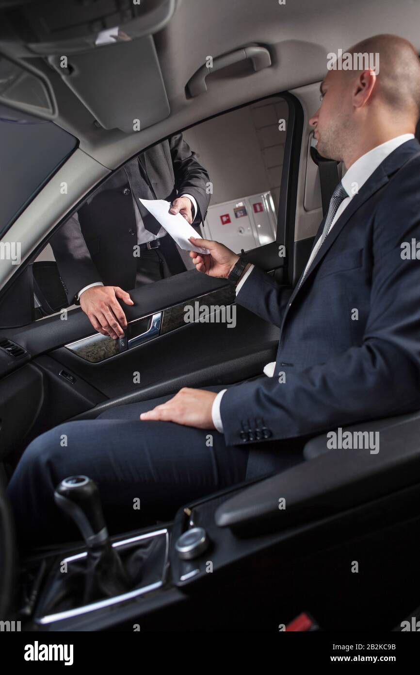 Young businessmen giving and receiving envelop through car window Stock ...