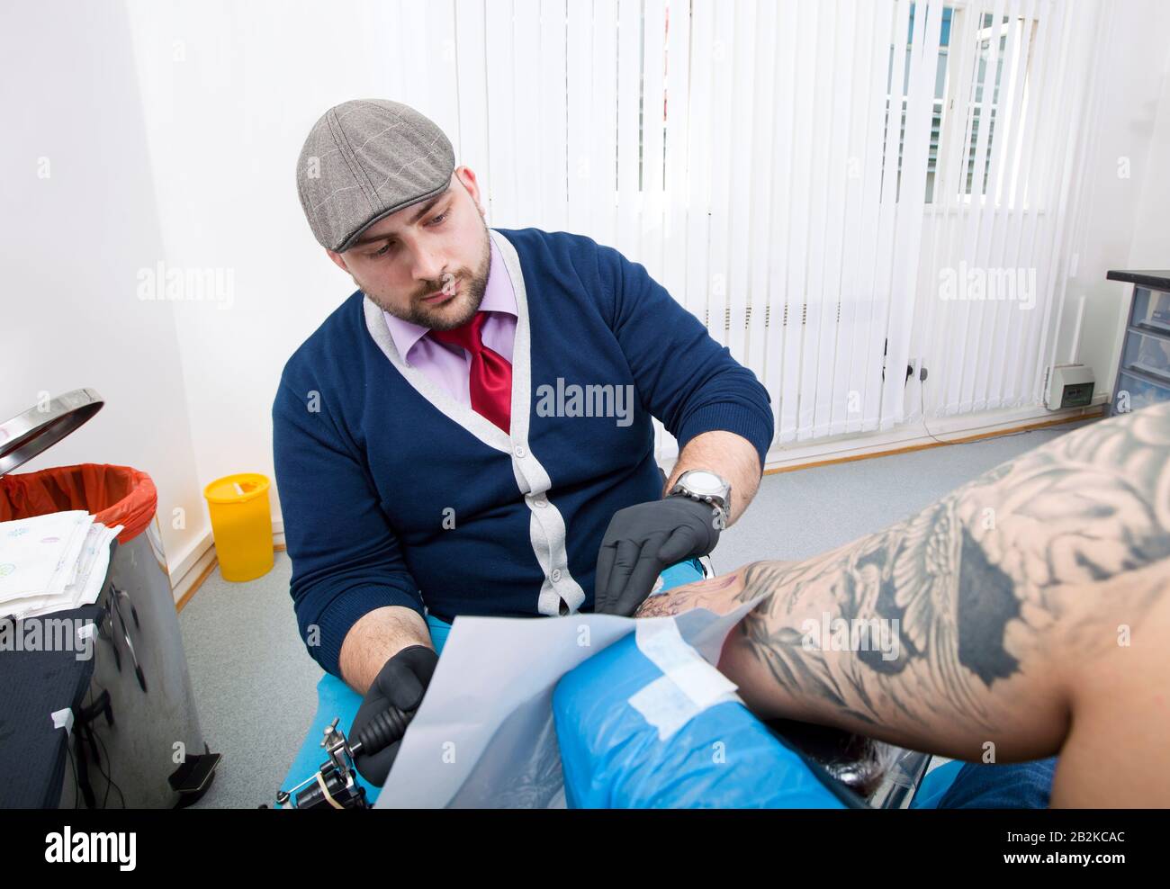 Young tattoo artist tattooing man's arm in studio Stock Photo - Alamy