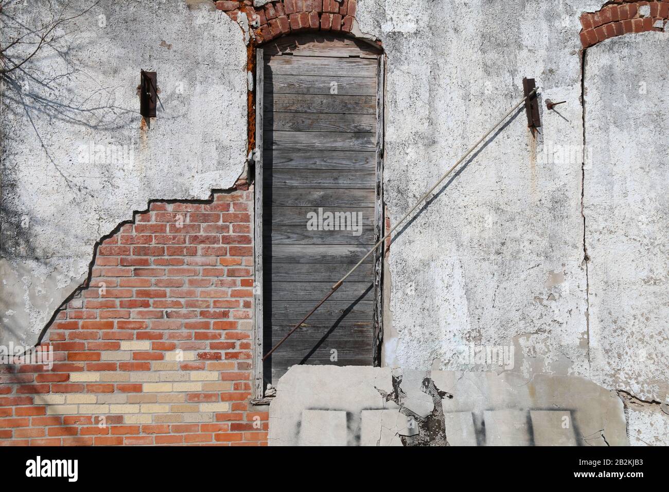 a boarded up arched window on a faded stucco red brick wall building ...