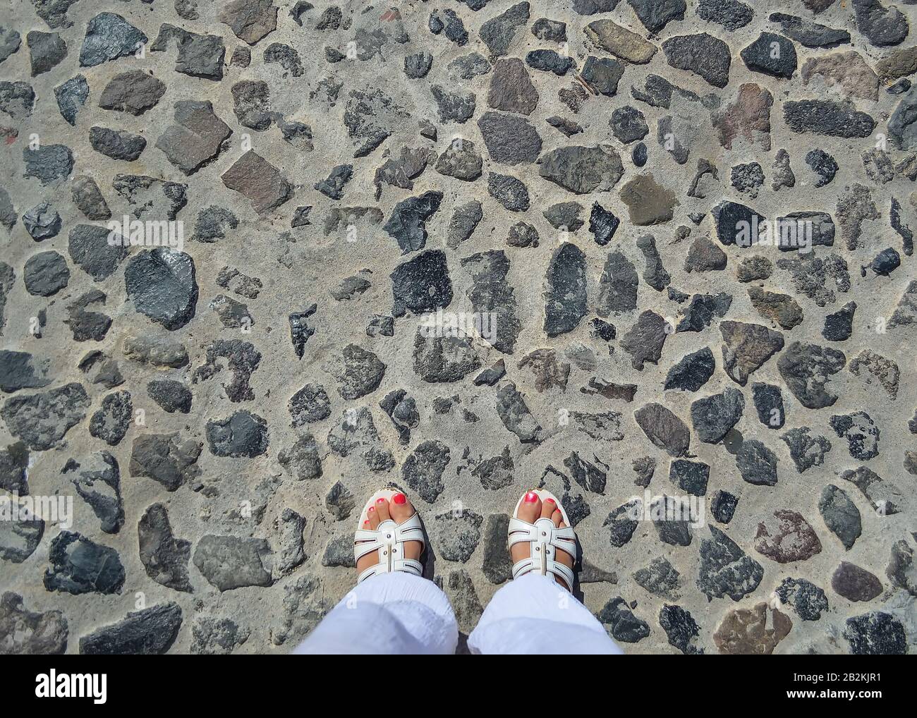 Female feet with red pedicure shoes in white sandals stand on the ...