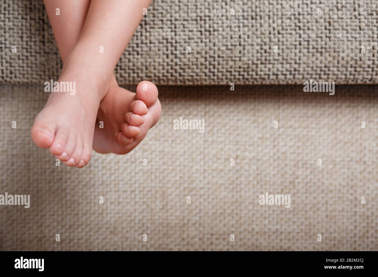 Children's legs close-up hanging from the sofa in the room. Baby toes ...