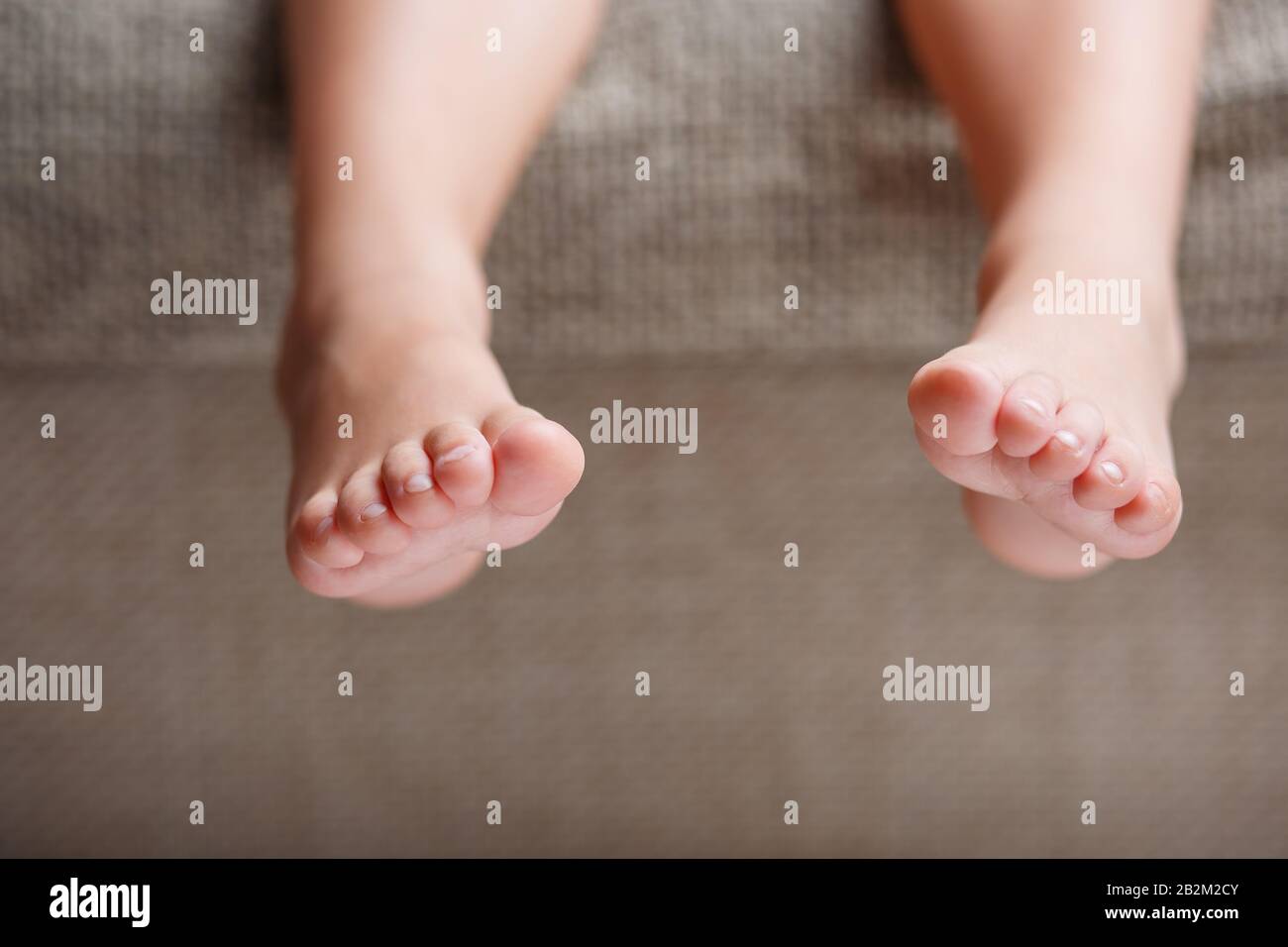 Children's legs close-up hanging from the sofa in the room. Baby toes ...