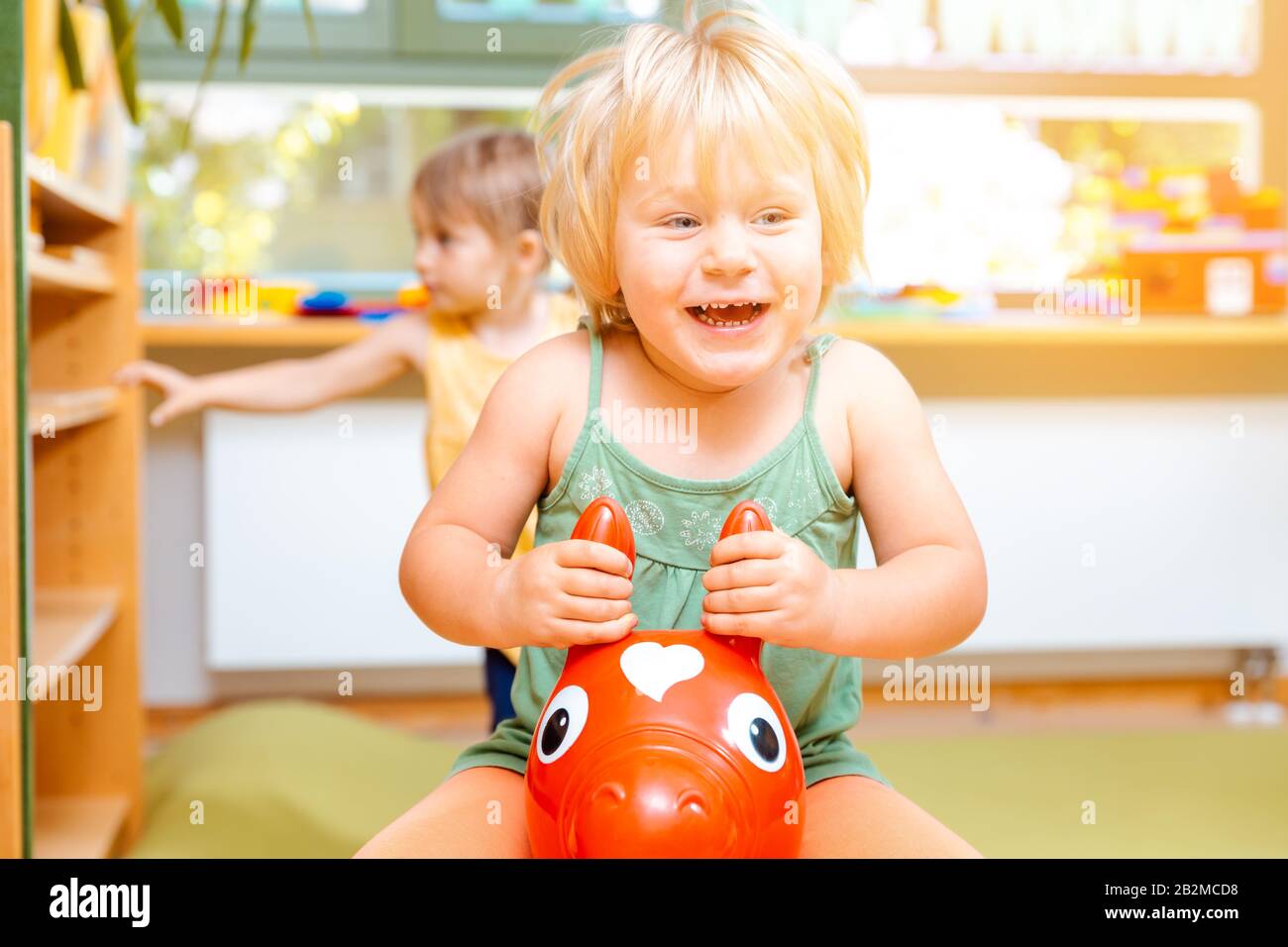 Little girls riding on play horses in kindergarten Stock Photo - Alamy