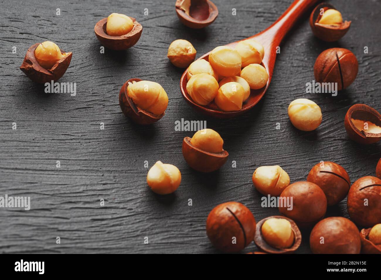Shelled macadamia nut and peeled macadamia nut on a black textural ...