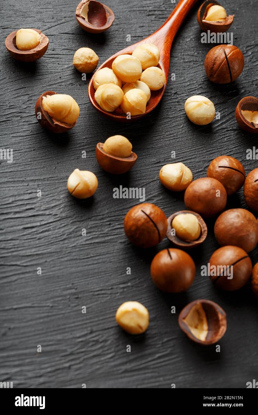 Shelled macadamia nut and peeled macadamia nut on a black textural ...