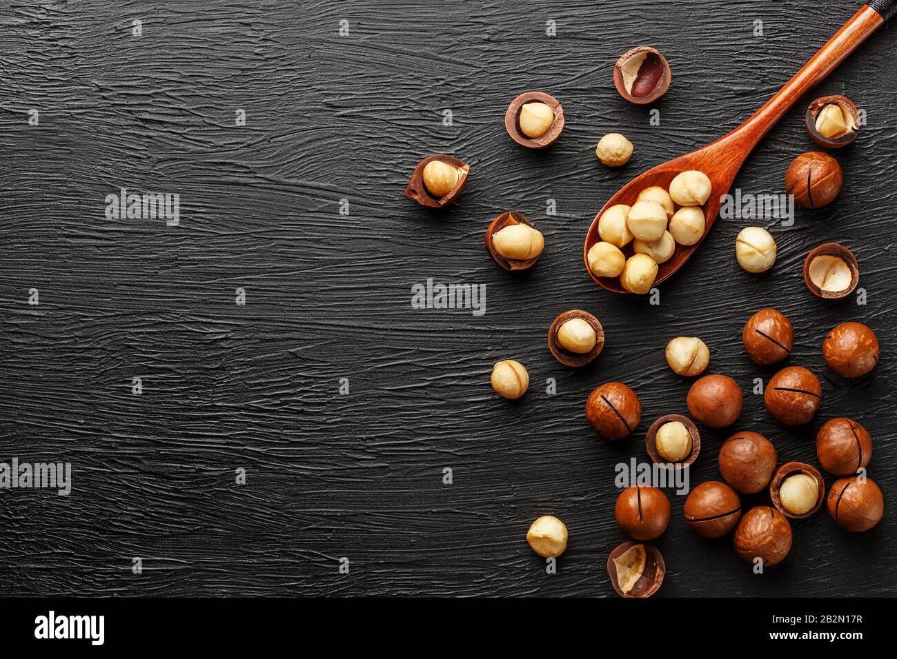 Shelled macadamia nut and peeled macadamia nut on a black textural ...