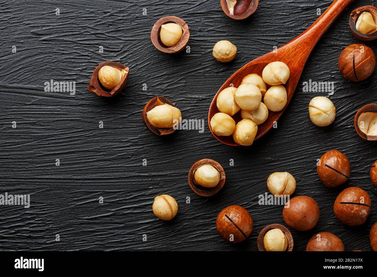 Shelled macadamia nut and peeled macadamia nut on a black textural ...