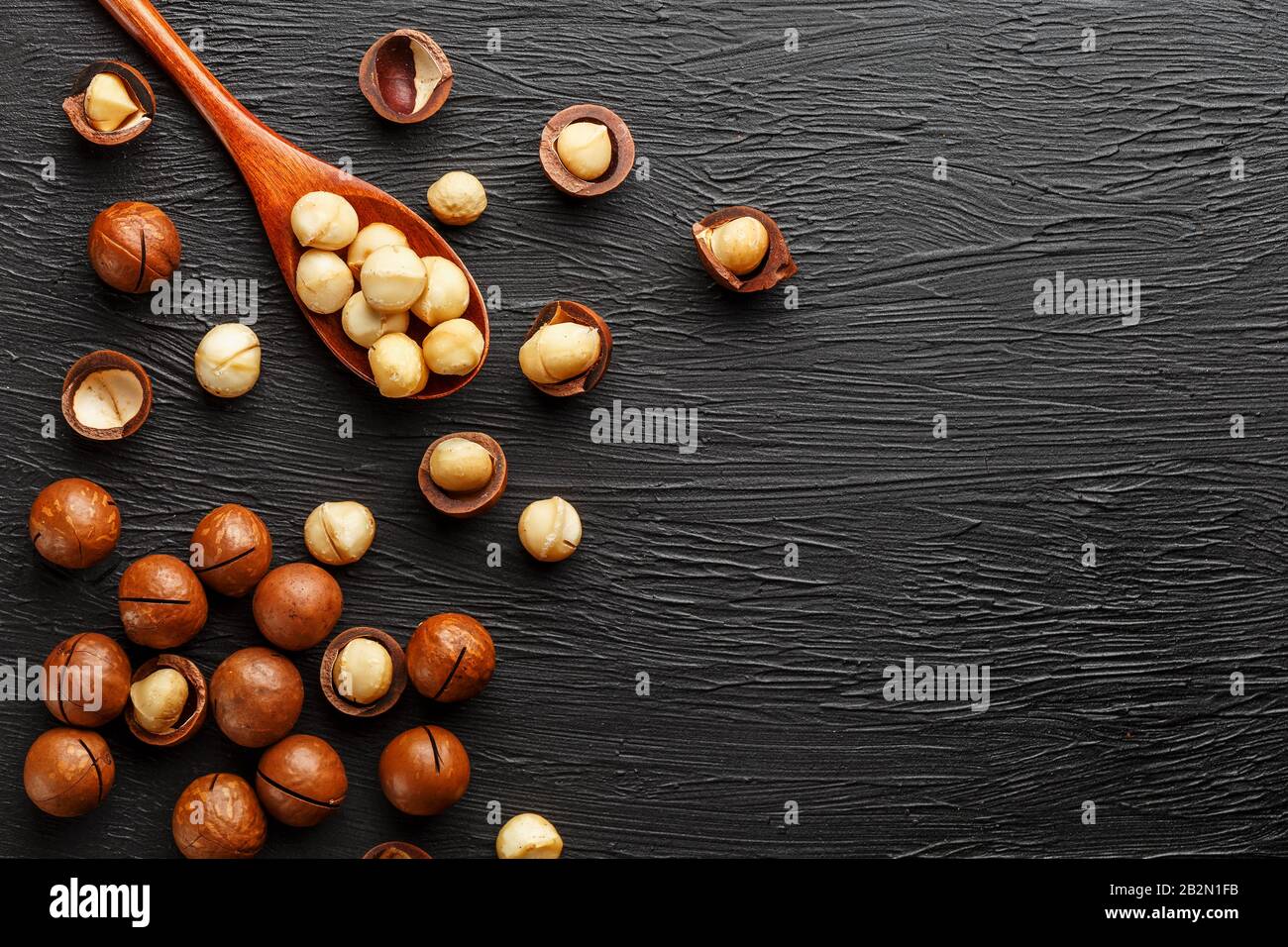 Shelled macadamia nut and peeled macadamia nut on a black textural ...