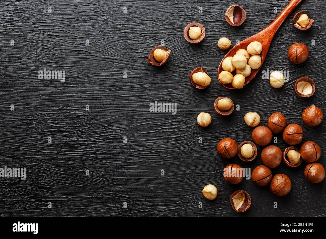 Shelled macadamia nut and peeled macadamia nut on a black textural ...