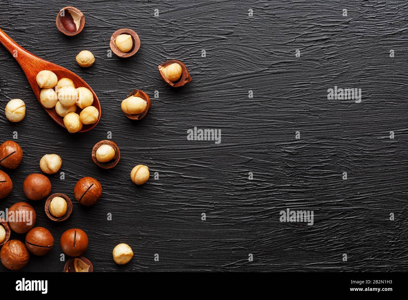 Shelled macadamia nut and peeled macadamia nut on a black textural ...