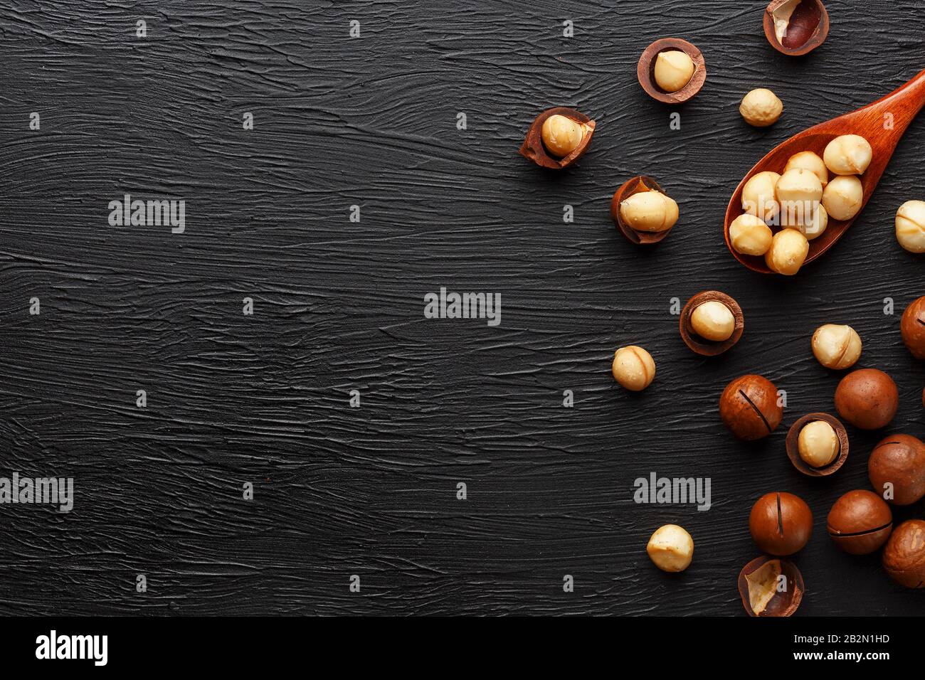 Shelled macadamia nut and peeled macadamia nut on a black textural ...