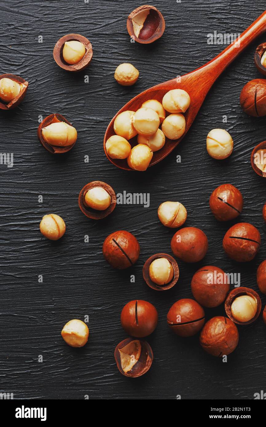 Shelled macadamia nut and peeled macadamia nut on a black textural ...