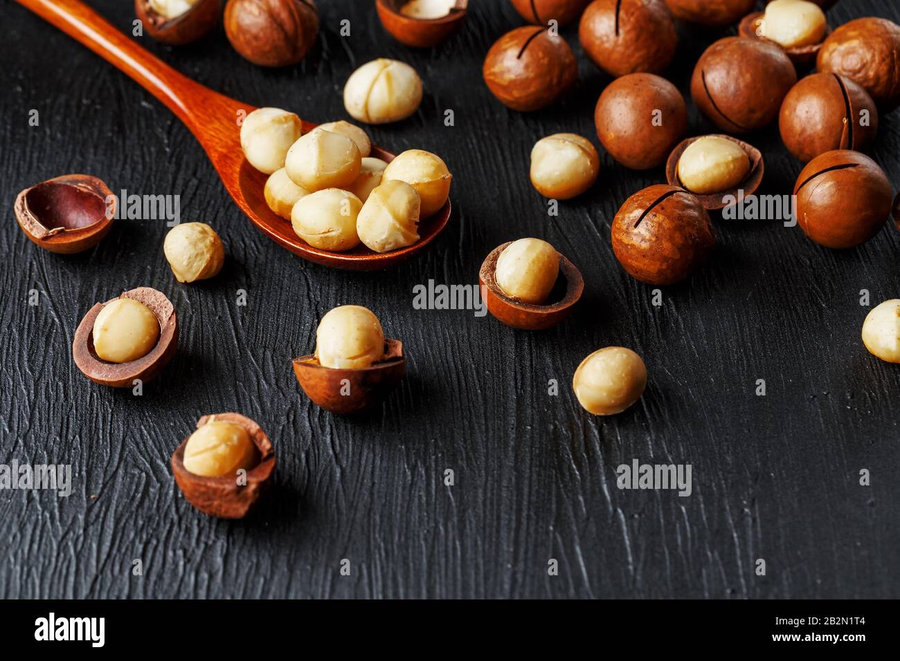 Shelled macadamia nut and peeled macadamia nut on a black textural ...