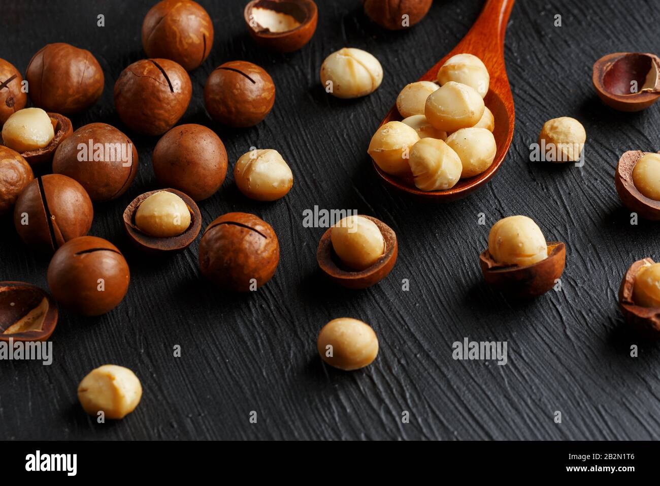Shelled macadamia nut and peeled macadamia nut on a black textural ...