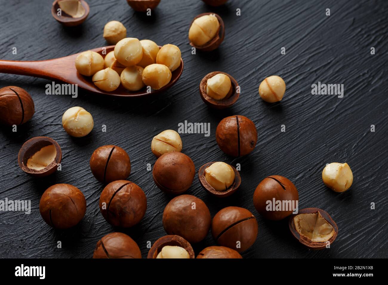 Shelled macadamia nut and peeled macadamia nut on a black textural ...