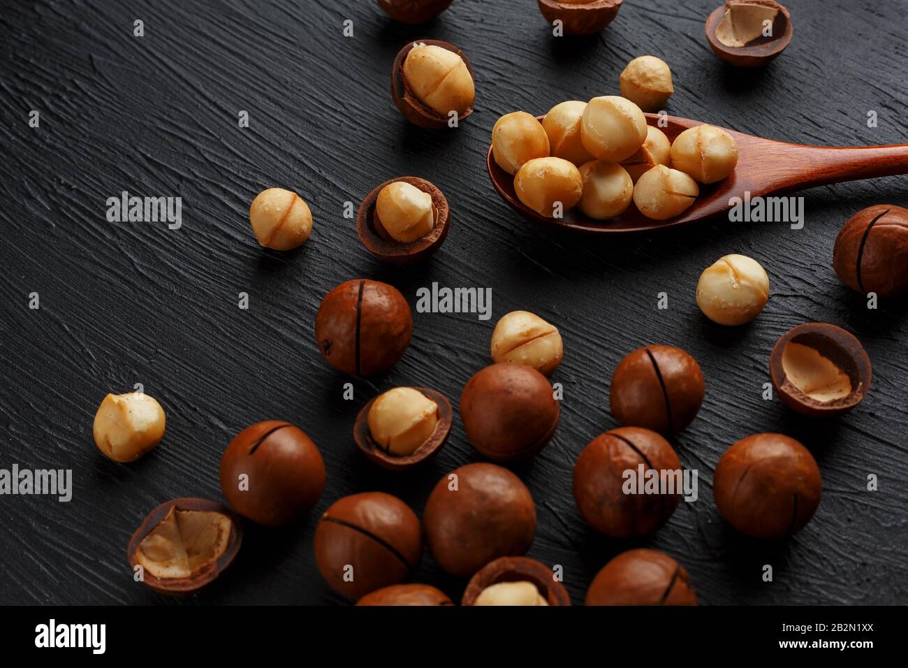 Shelled macadamia nut and peeled macadamia nut on a black textural ...