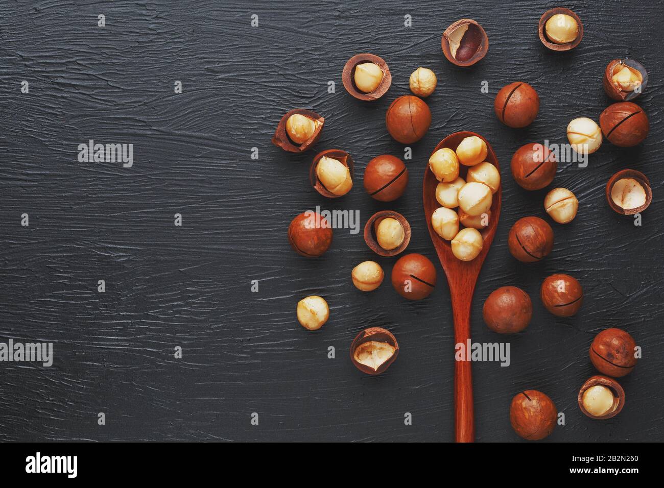 Shelled macadamia nut and peeled macadamia nut on a black textural ...