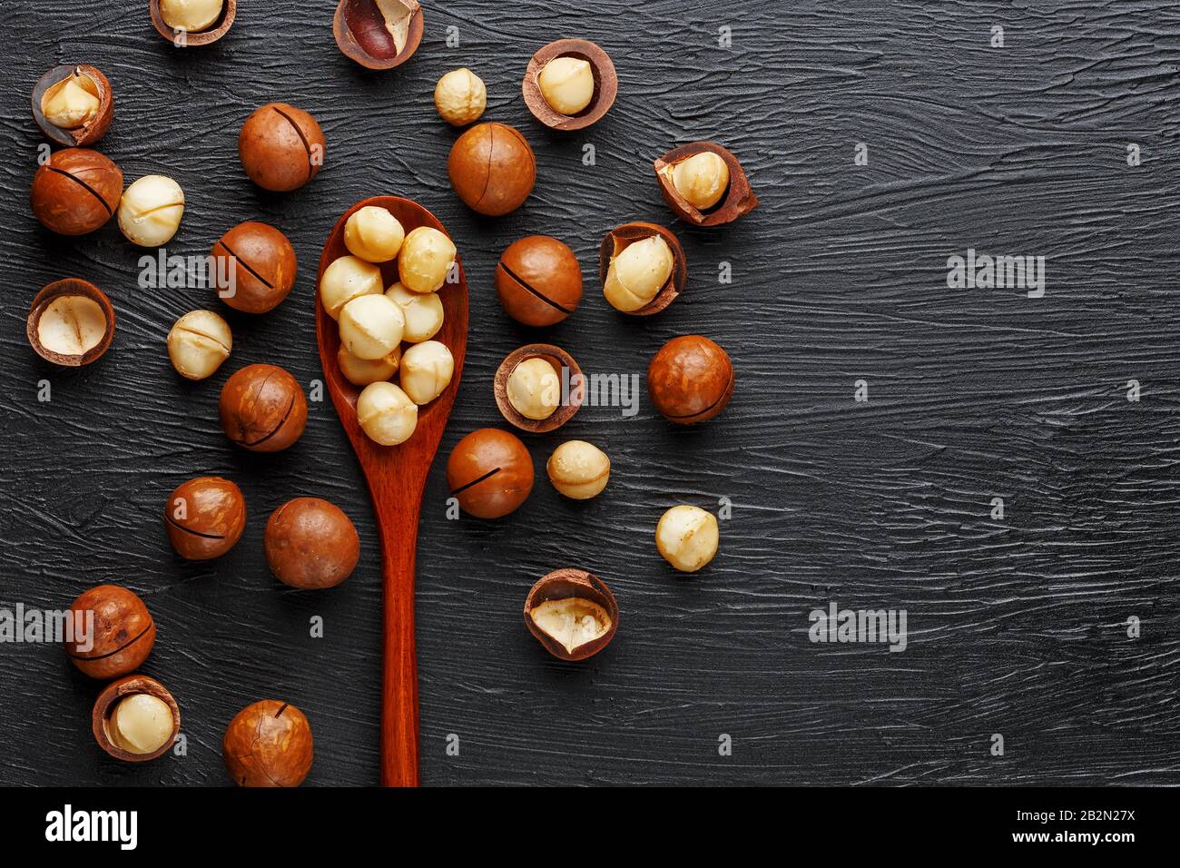 Shelled macadamia nut and peeled macadamia nut on a black textural ...