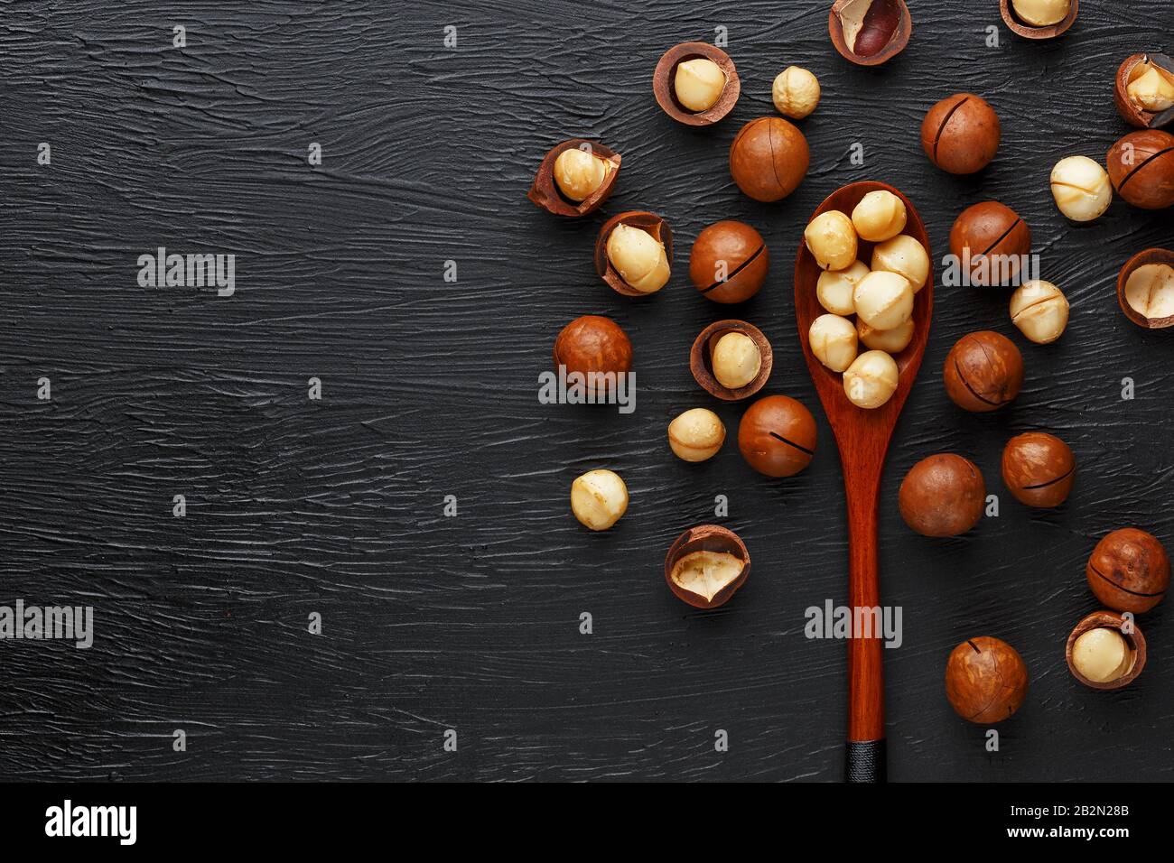 Shelled macadamia nut and peeled macadamia nut on a black textural ...