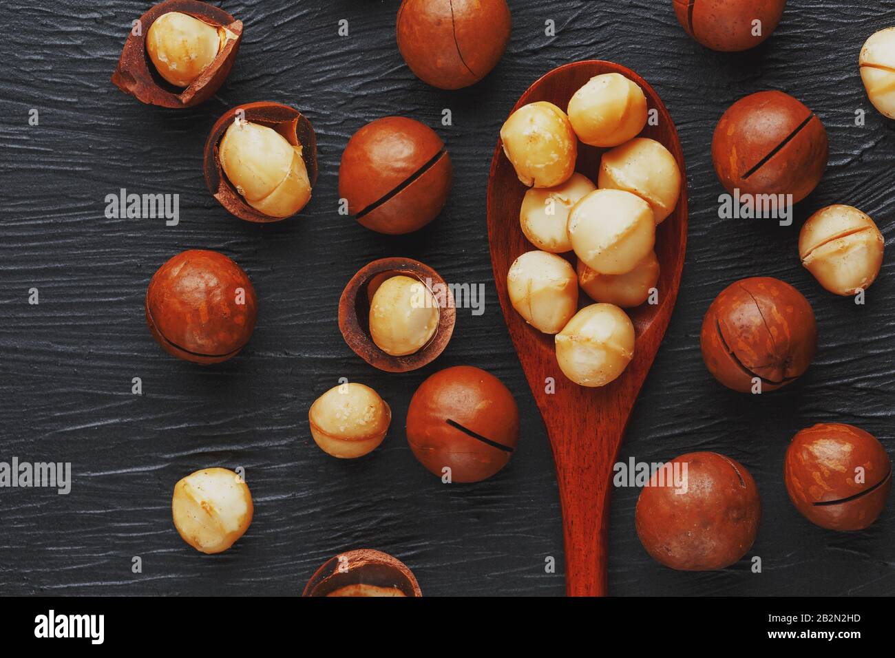 Shelled macadamia nut and peeled macadamia nut on a black textural ...