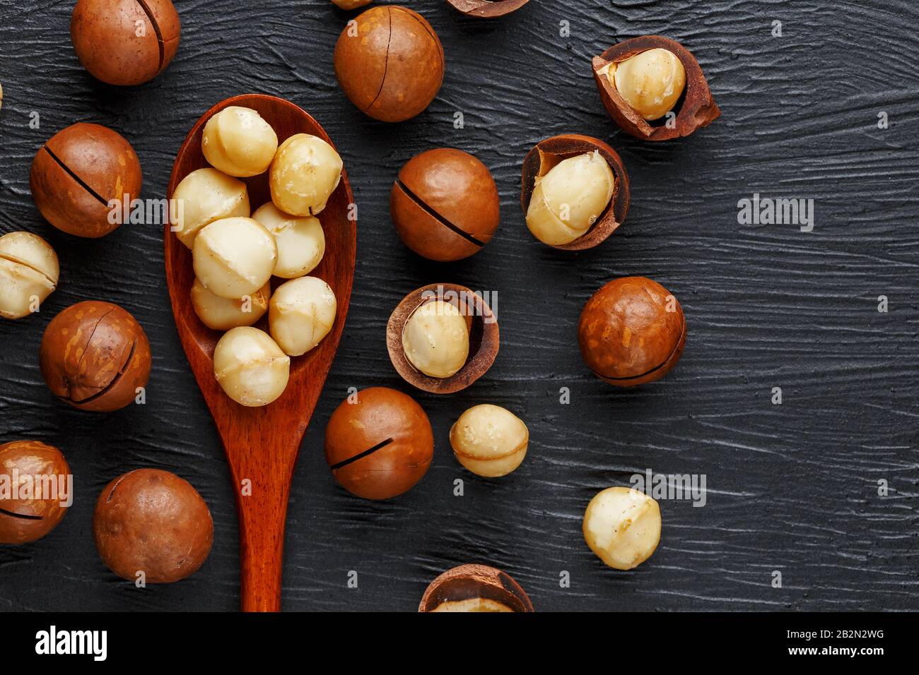 Shelled macadamia nut and peeled macadamia nut on a black textural ...