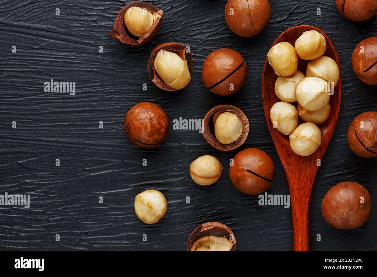 Shelled macadamia nut and peeled macadamia nut on a black textural ...