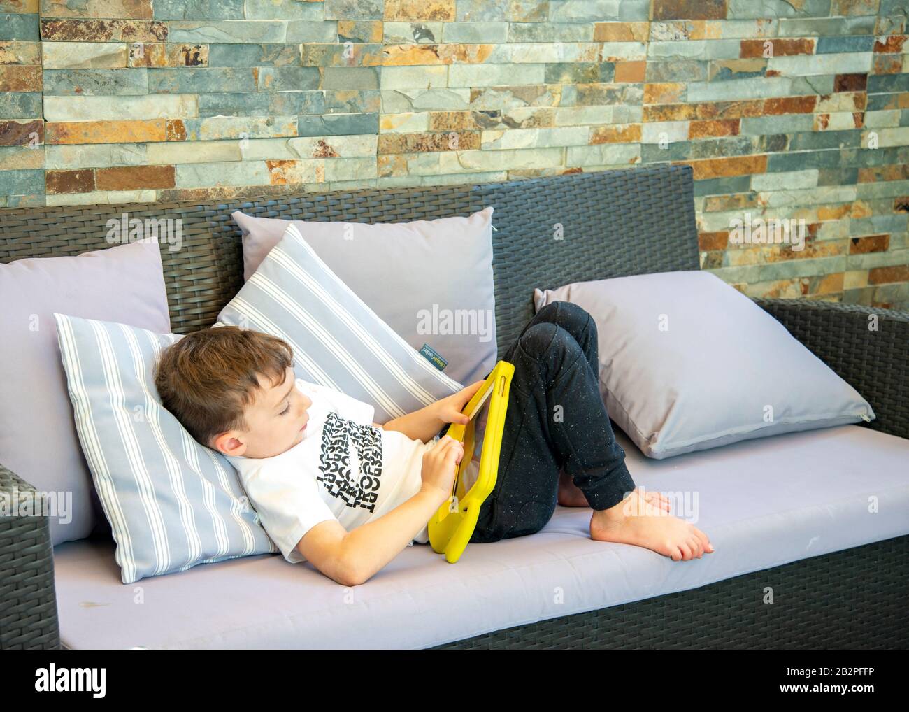 Young boy relaxing on garden furniture using his tablet Stock Photo - Alamy