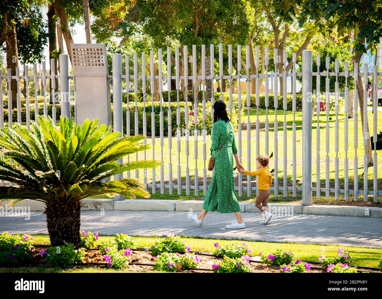 Mother and child walking hand in hand along palm lined walkway in ...