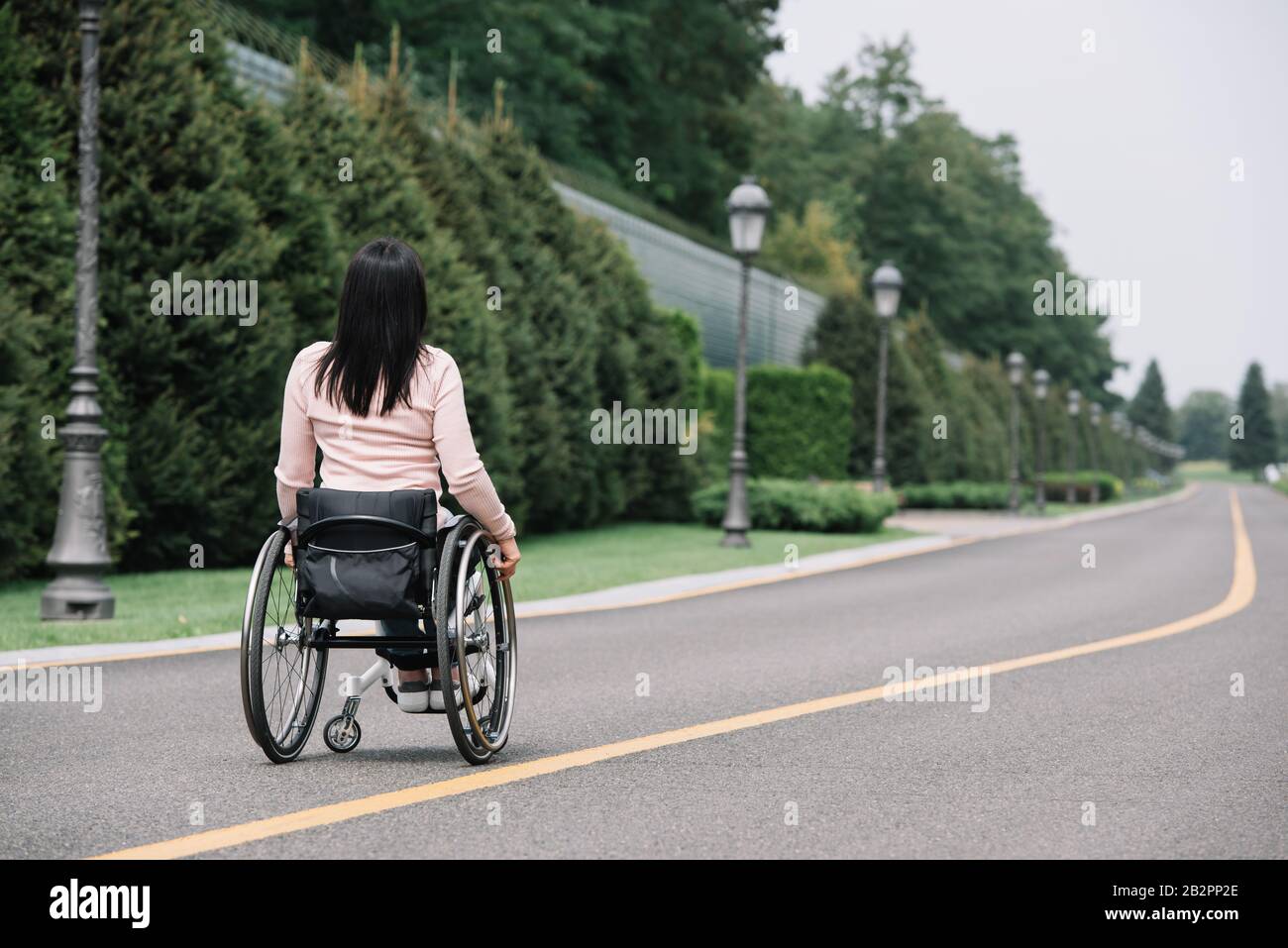 back view of young disabled woman walking in park in wheelchair Stock ...
