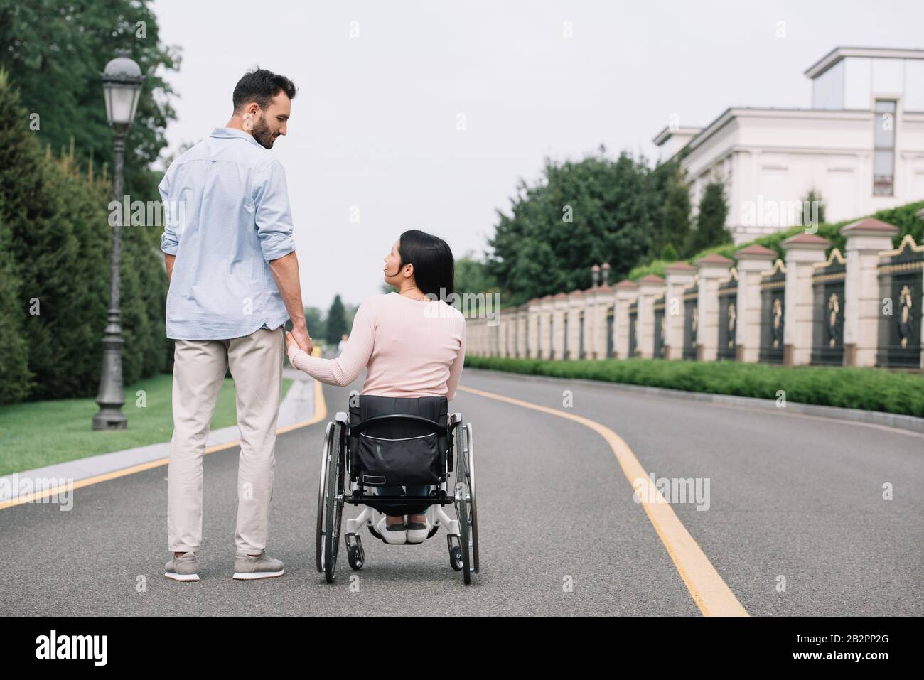 back view of young man and disabled woman holding hands while walking ...