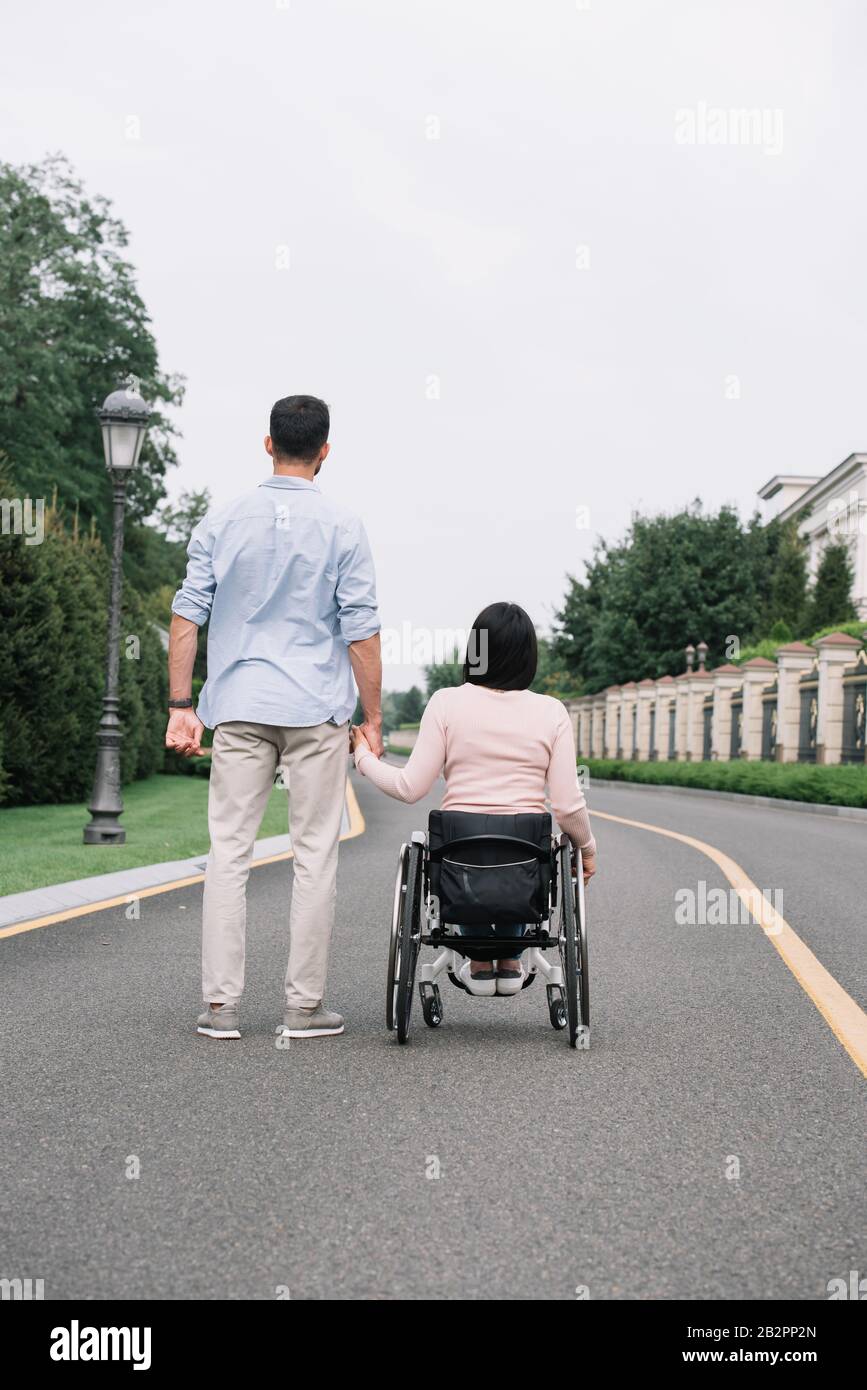 back view of young man holding hands with disabled girlfriend while ...