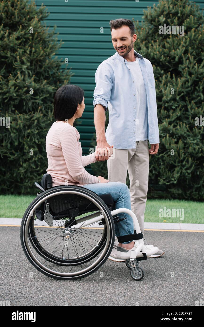happy man holding hands with disabled girlfriend while walking in park ...