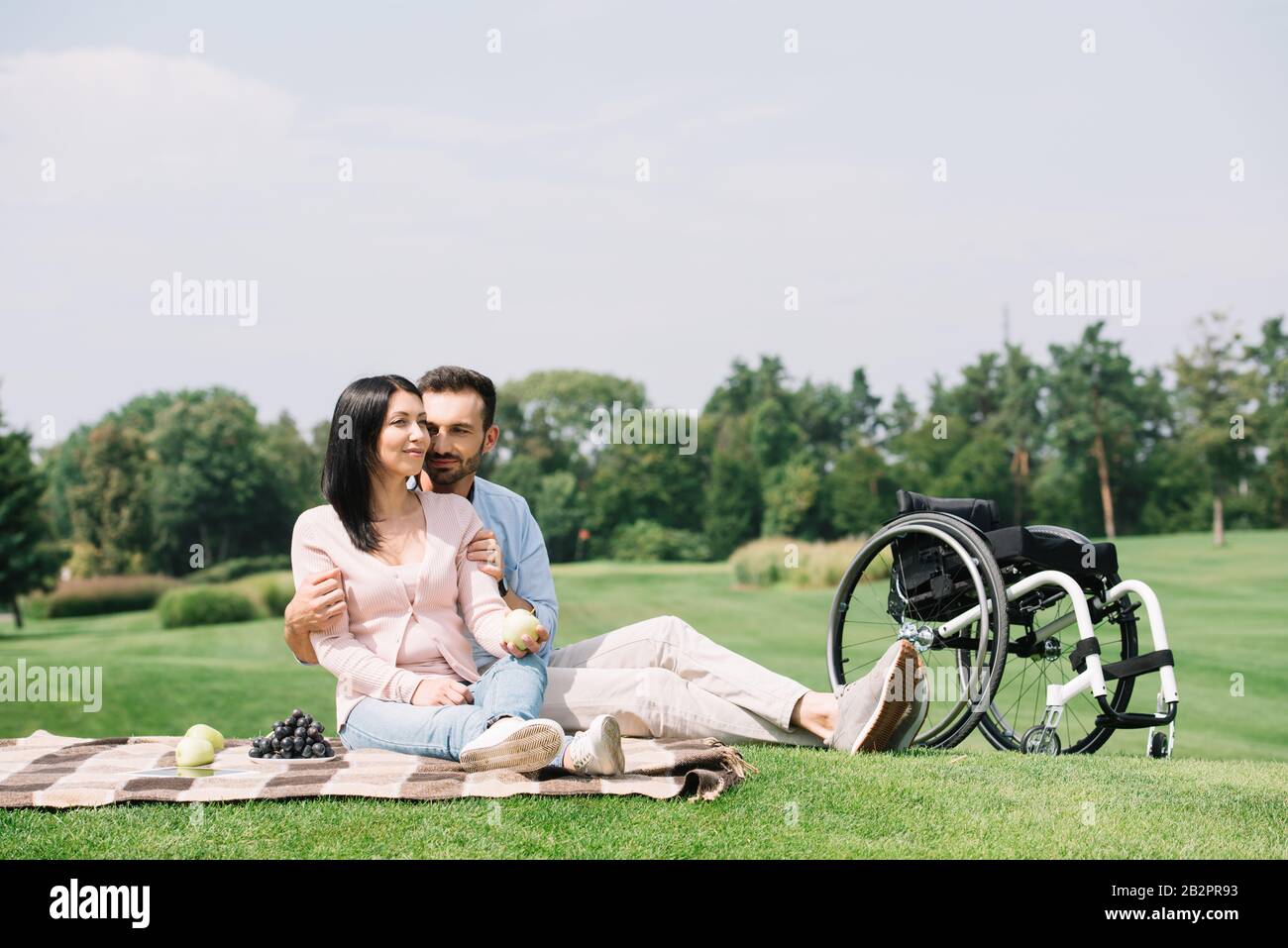 happy handsome man hugging young disabled girlfriend while sitting on ...