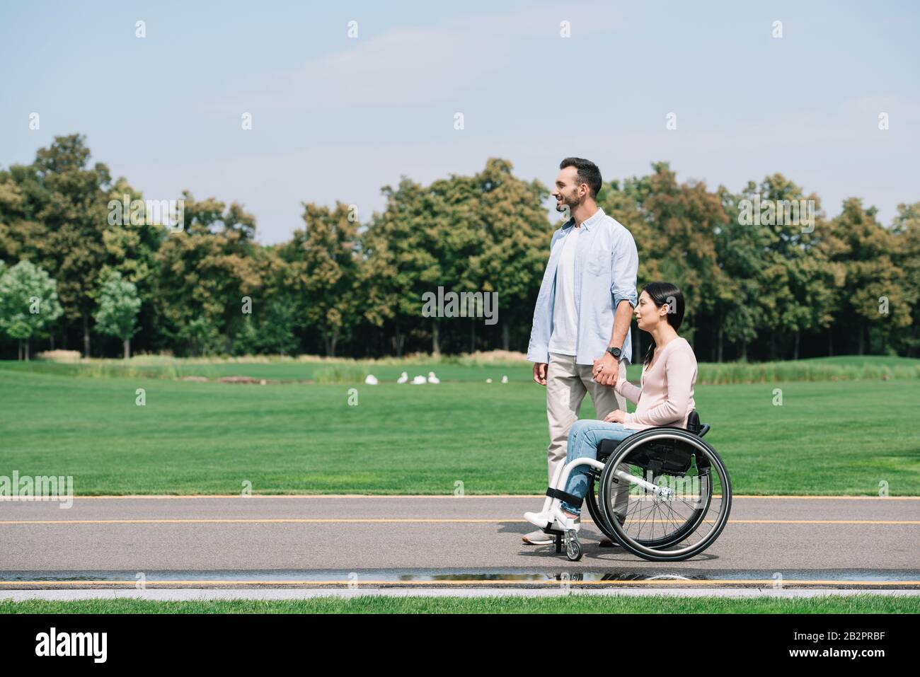 handsome young man holding hands with disabled girlfriend while walking ...