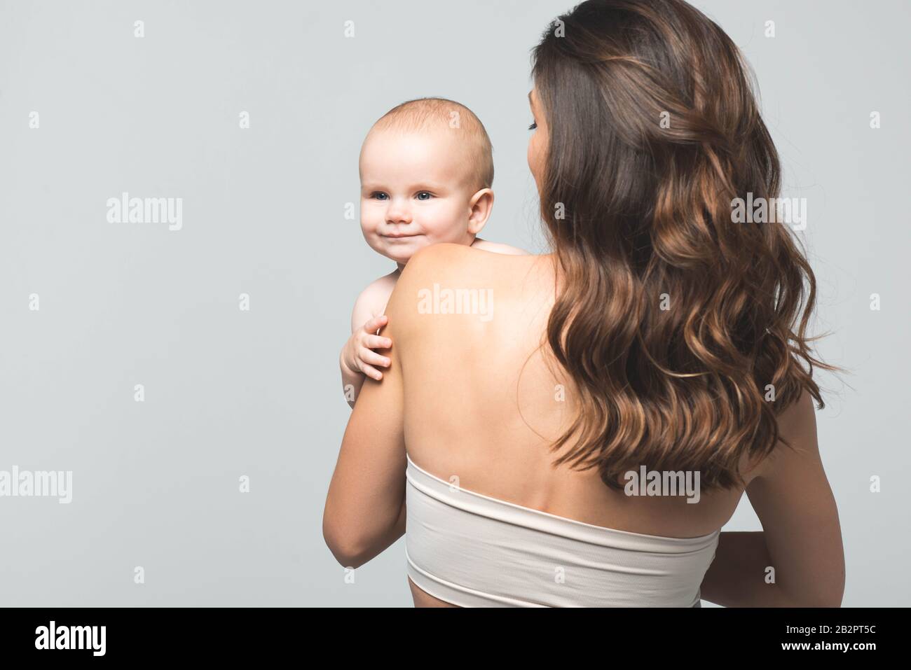 back view of young mother holding baby boy, isolated on grey Stock ...