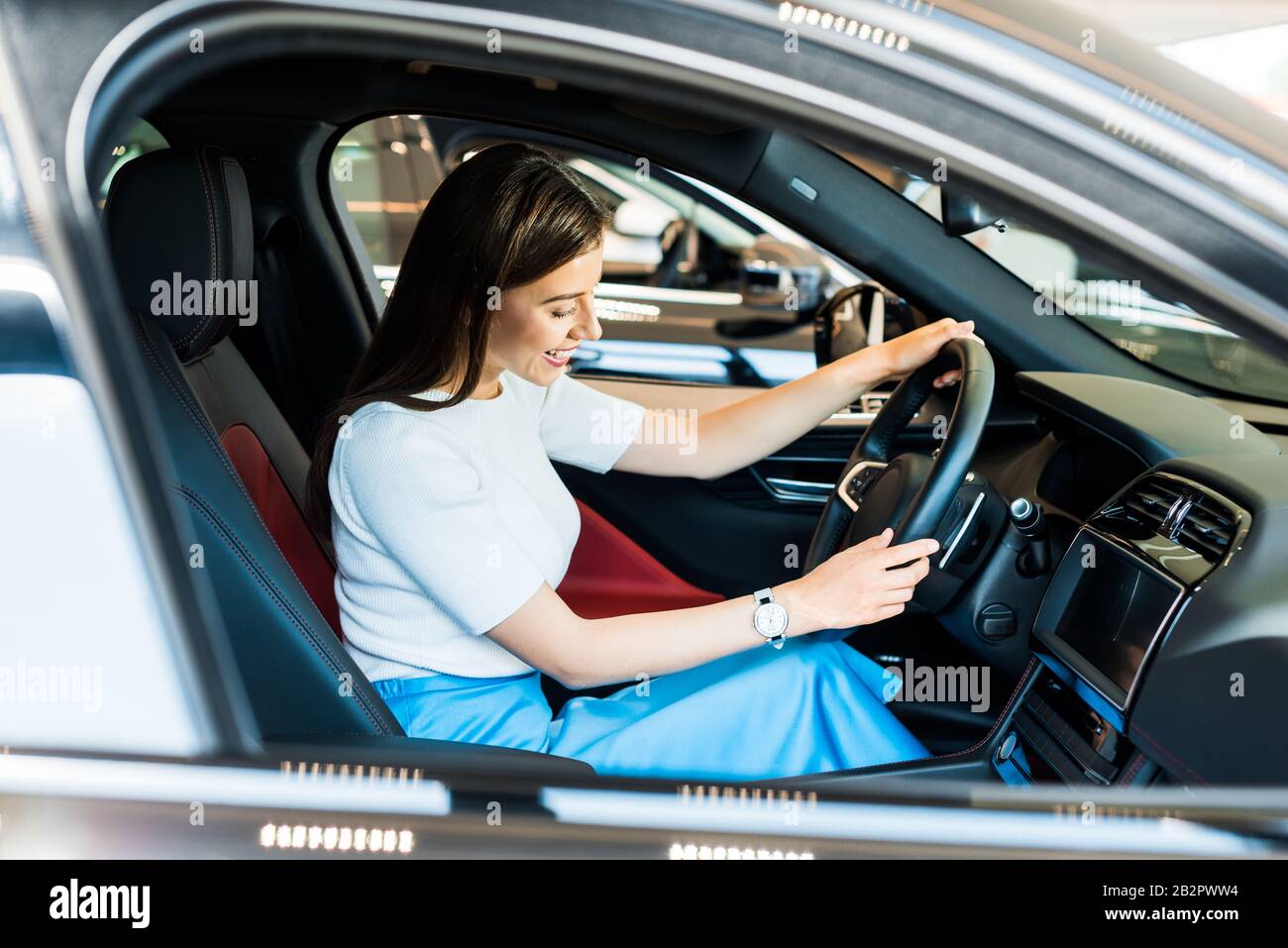 selective focus of smiling woman touching steering wheel while sitting ...