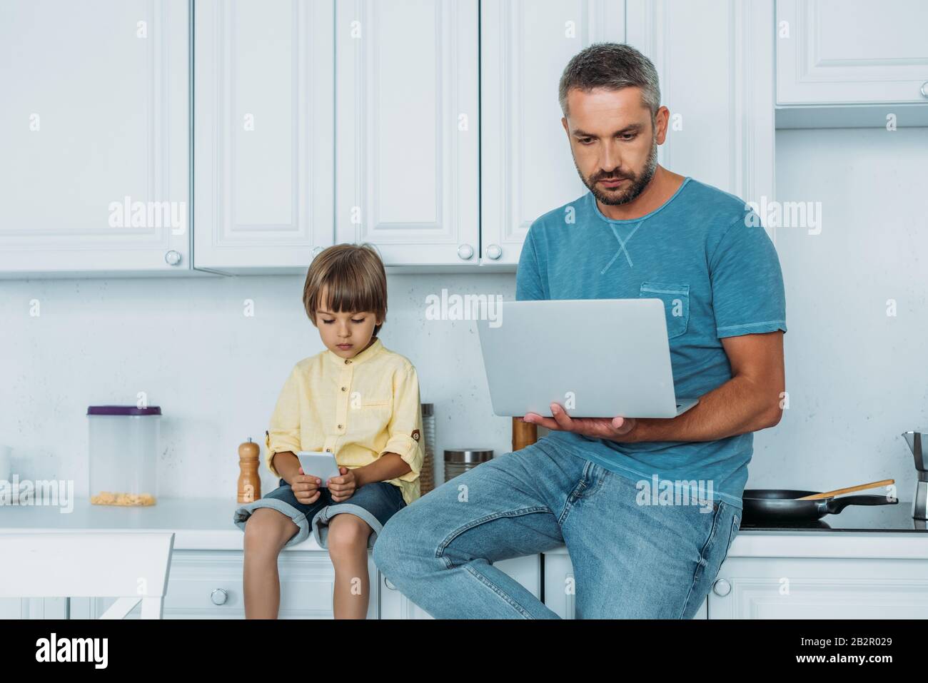 father using laptop and and son using smartphone while sitting on ...