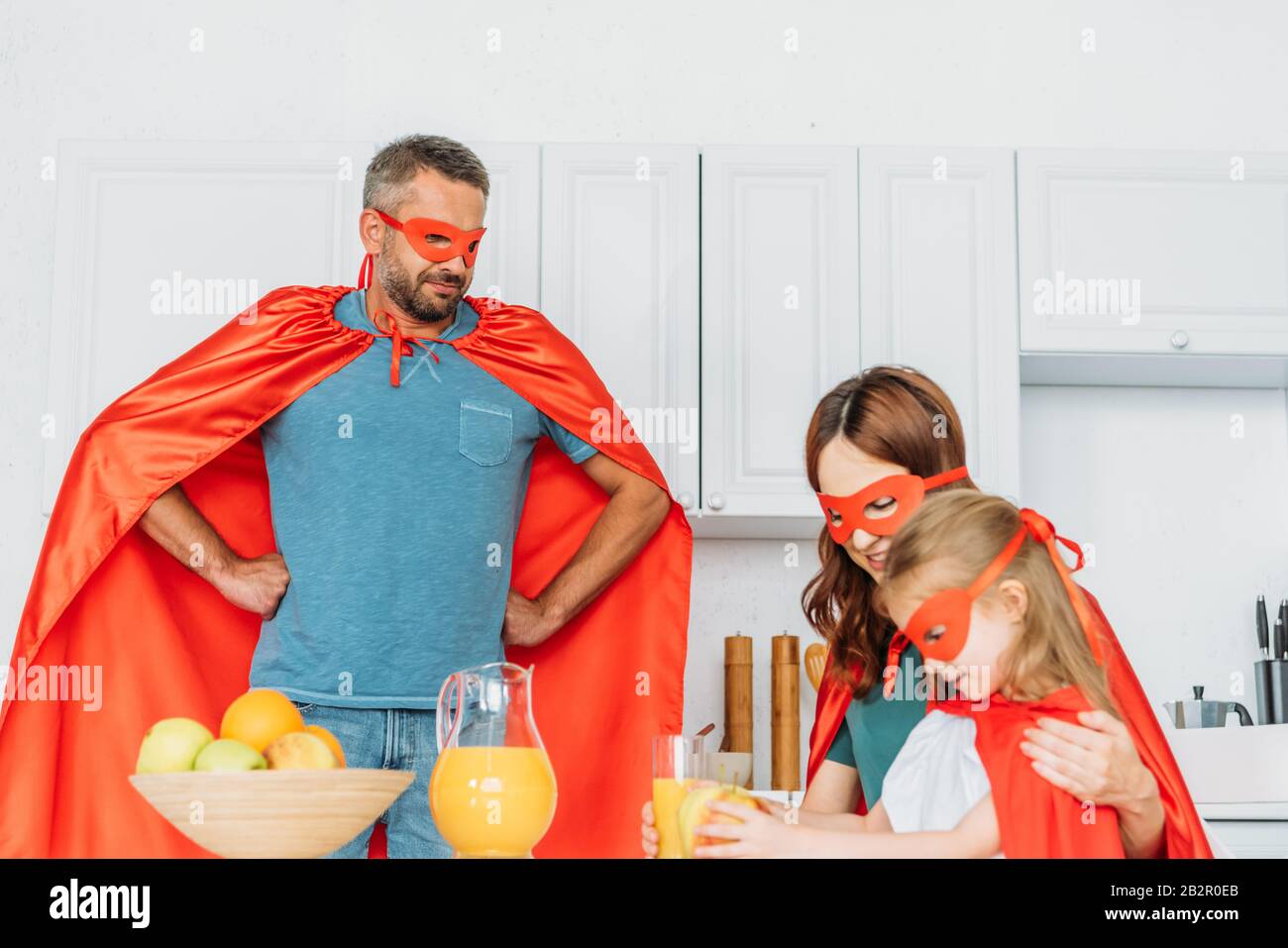 family in superhero costumes having breakfast in kitchen while father ...