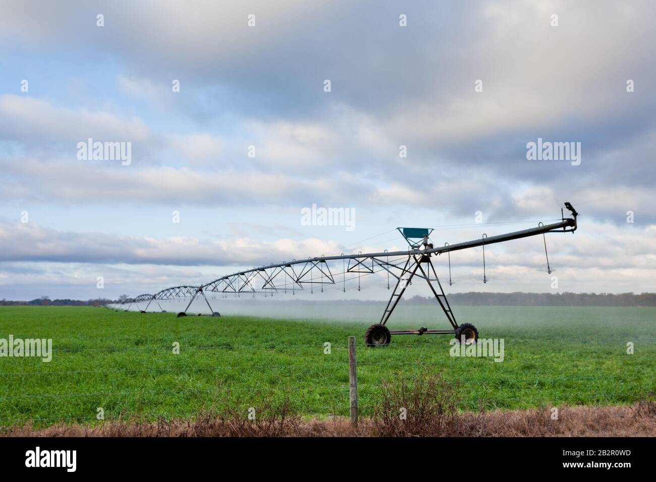 Irrigation system at work in a green hayfield under the cloudy sky ...