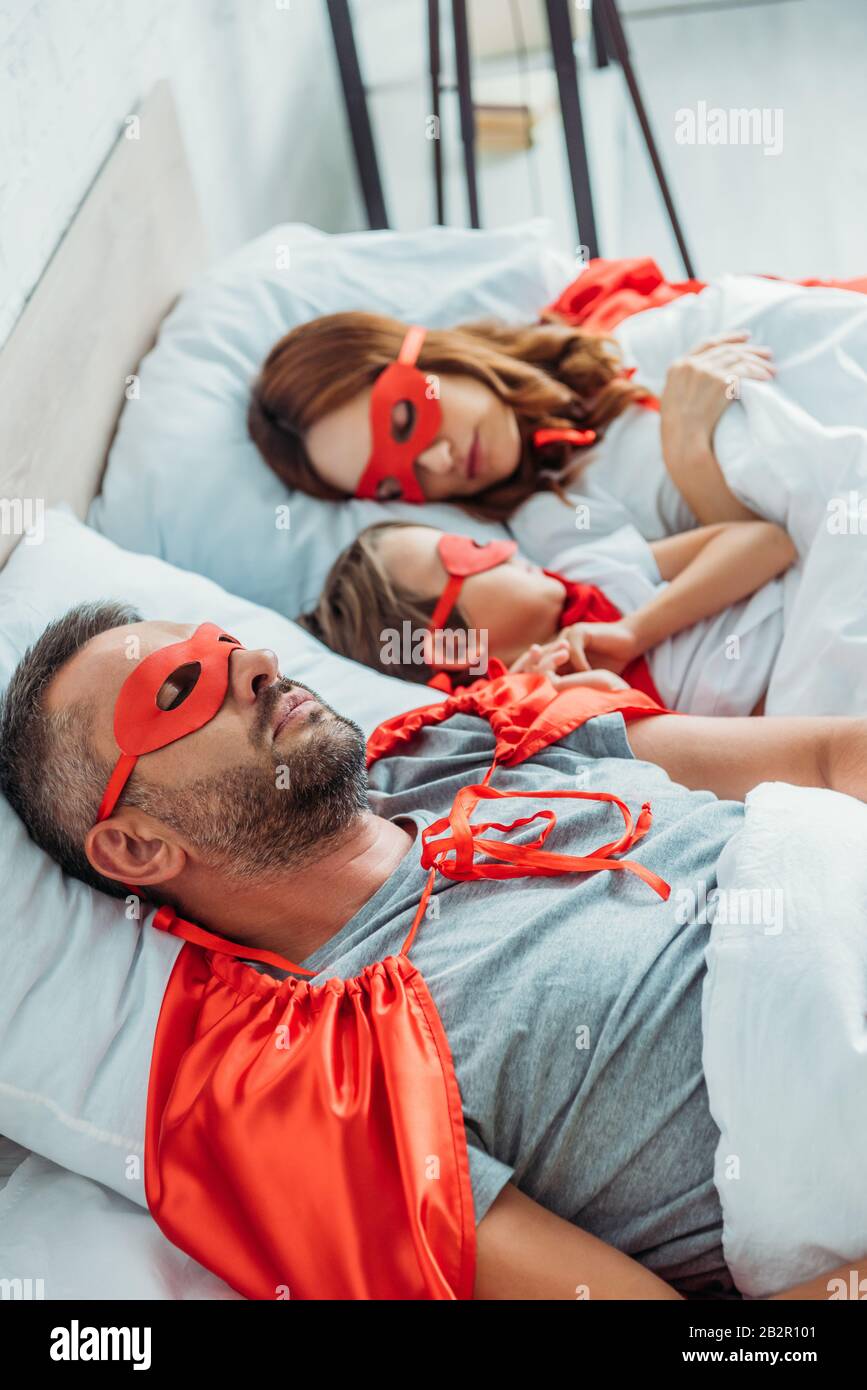 selective focus of mom, dad and son sleeping in bed in superheroes ...