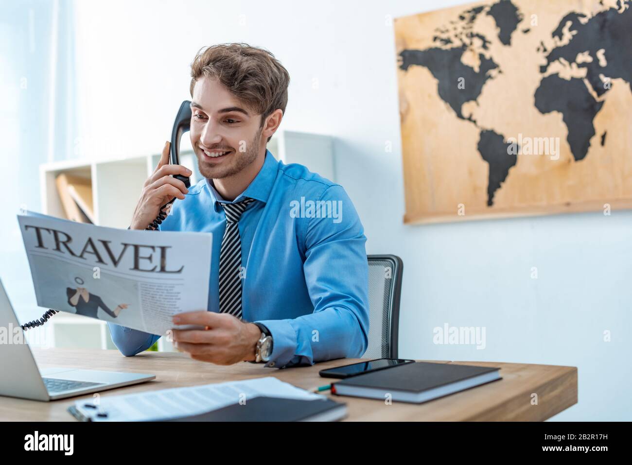 smiling travel agent talking on phone while holding travel newspaper ...