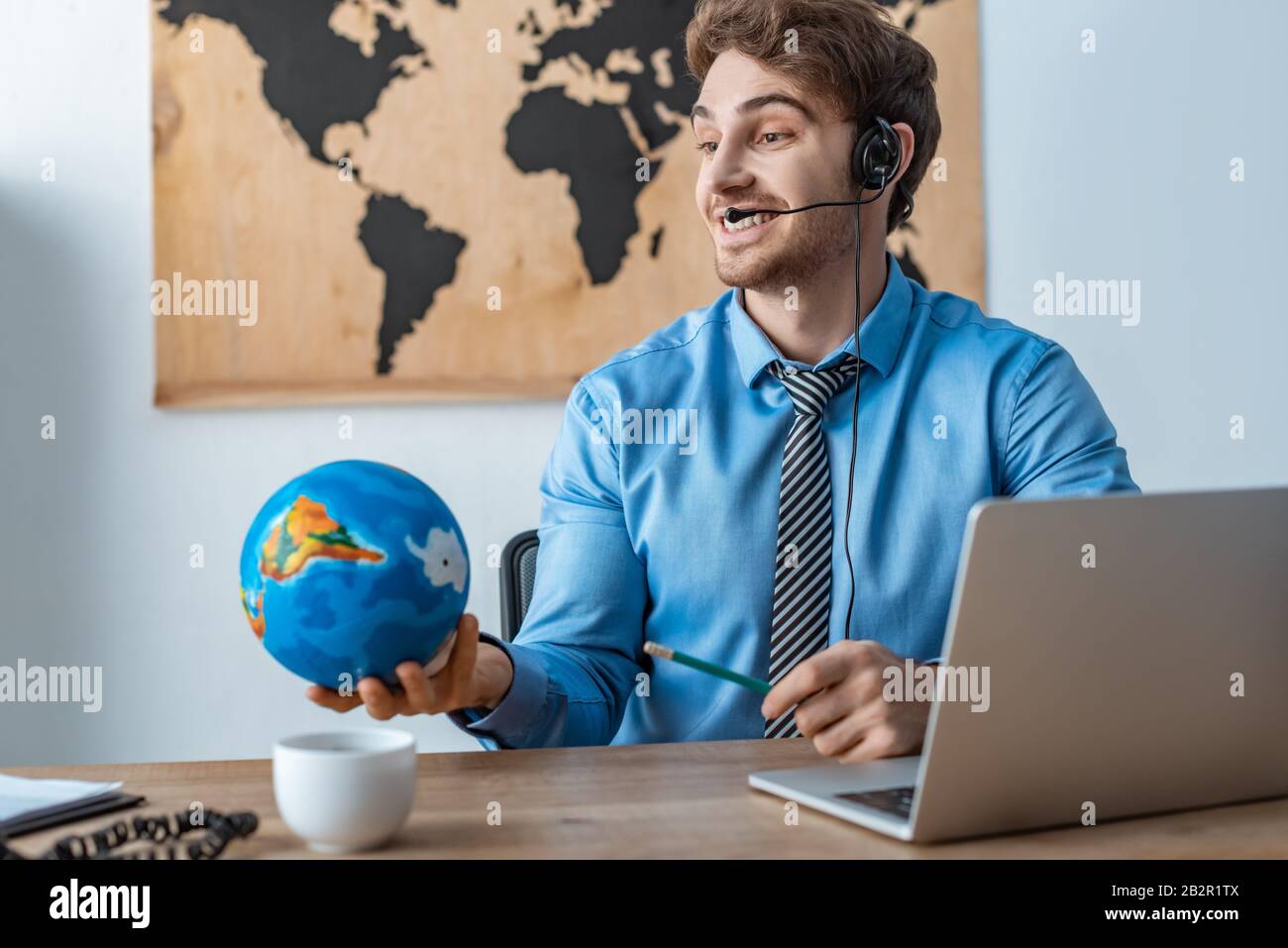 smiling travel agent holding globe while sitting at workplace Stock ...
