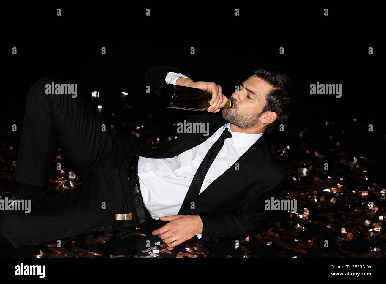 elegant man drinking champagne from bottle while lying on floor with ...