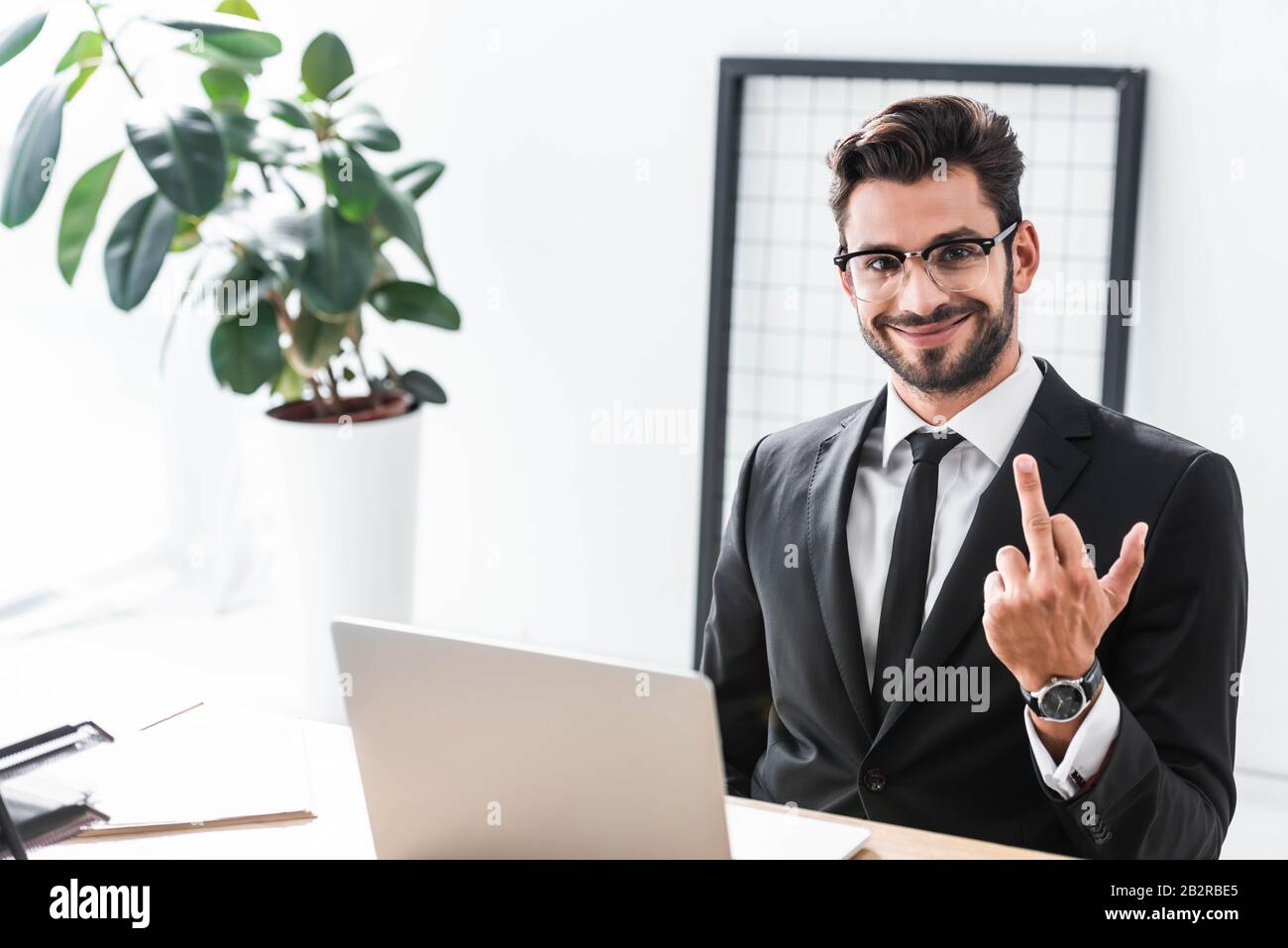 Smiling businessman showing middle finger gesture at office table Stock ...